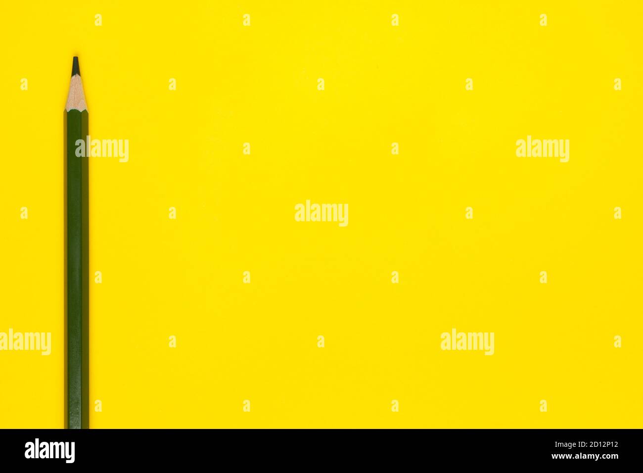 vertical dark green sharp wooden pencil on a bright yellow background ...