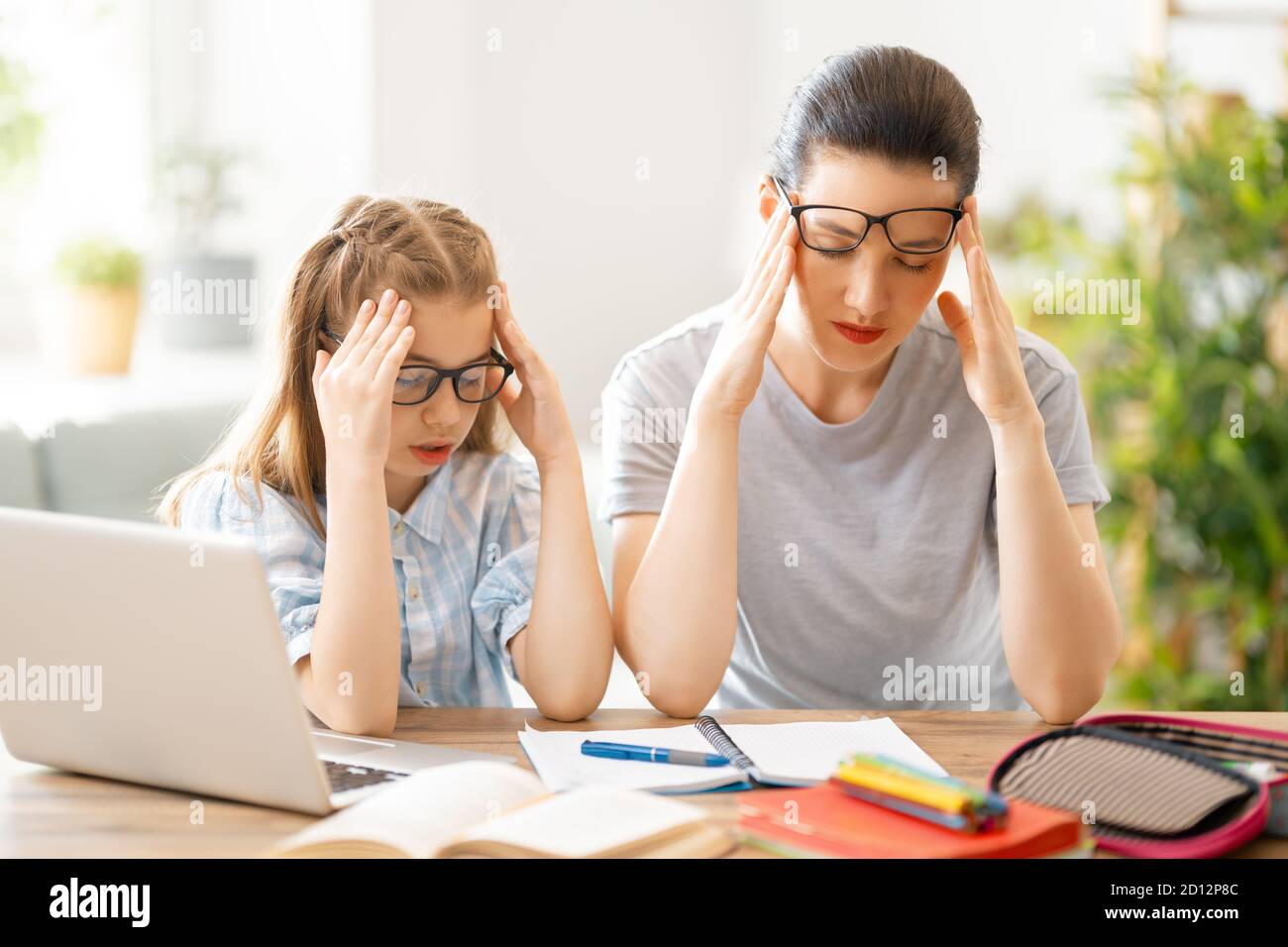 Back to school. Unhappy child and adult are sitting at desk. Girl doing ...