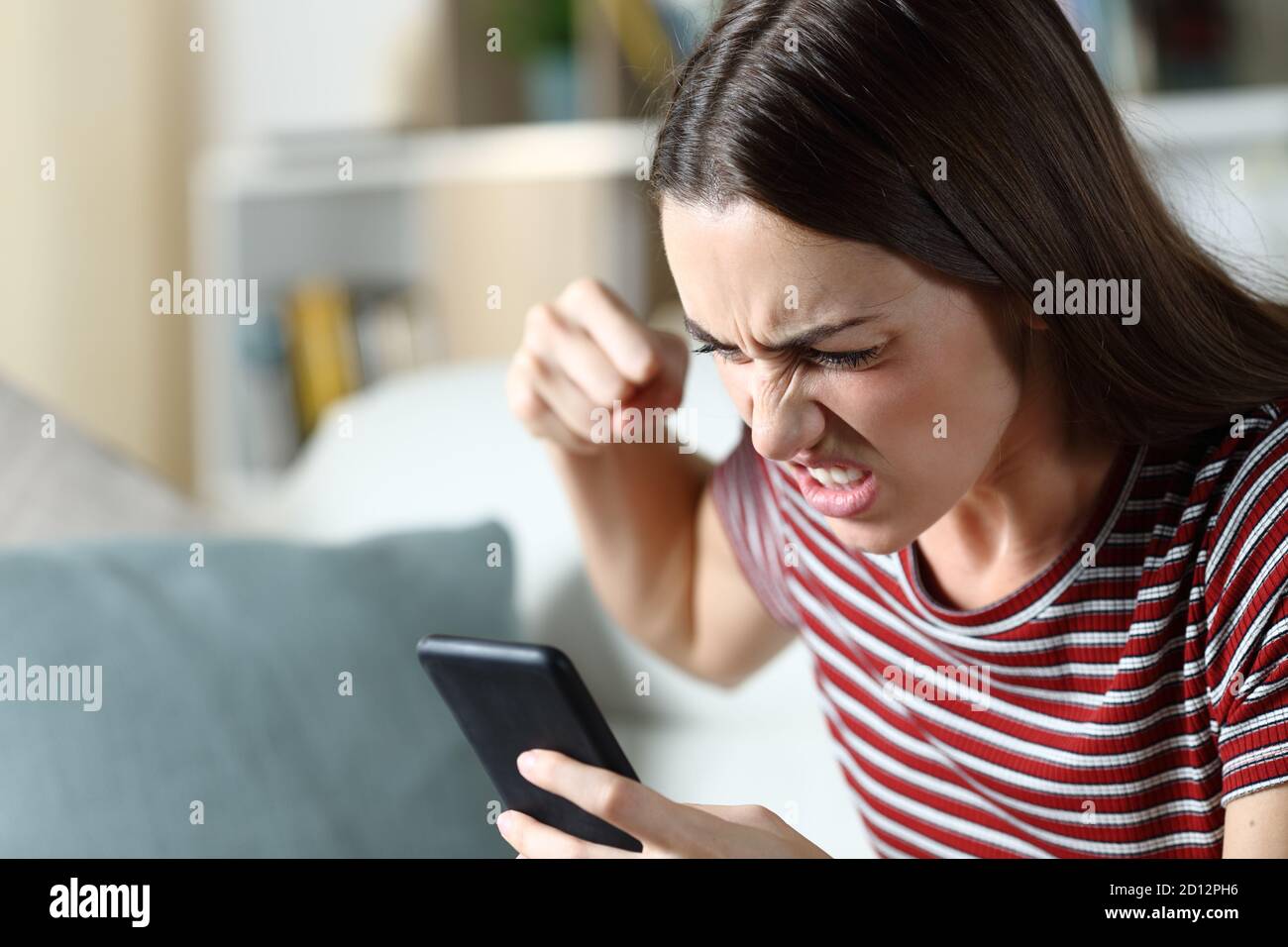 Angry woman checking smart phone sitting on a couch at home Stock Photo ...