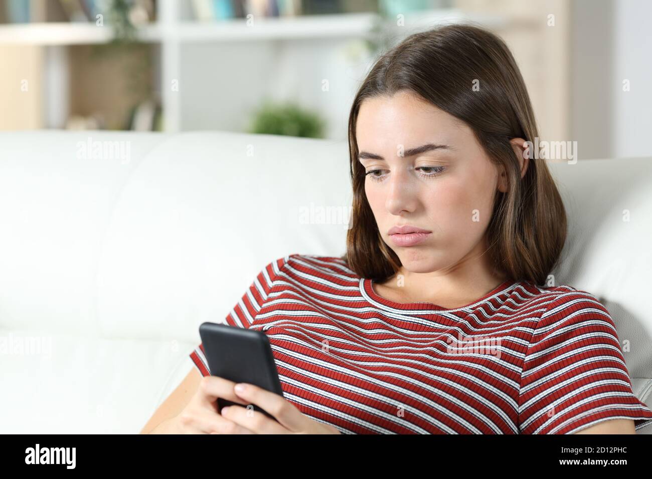 Bored teen checking smart phone content sitting on a sofa at home Stock ...