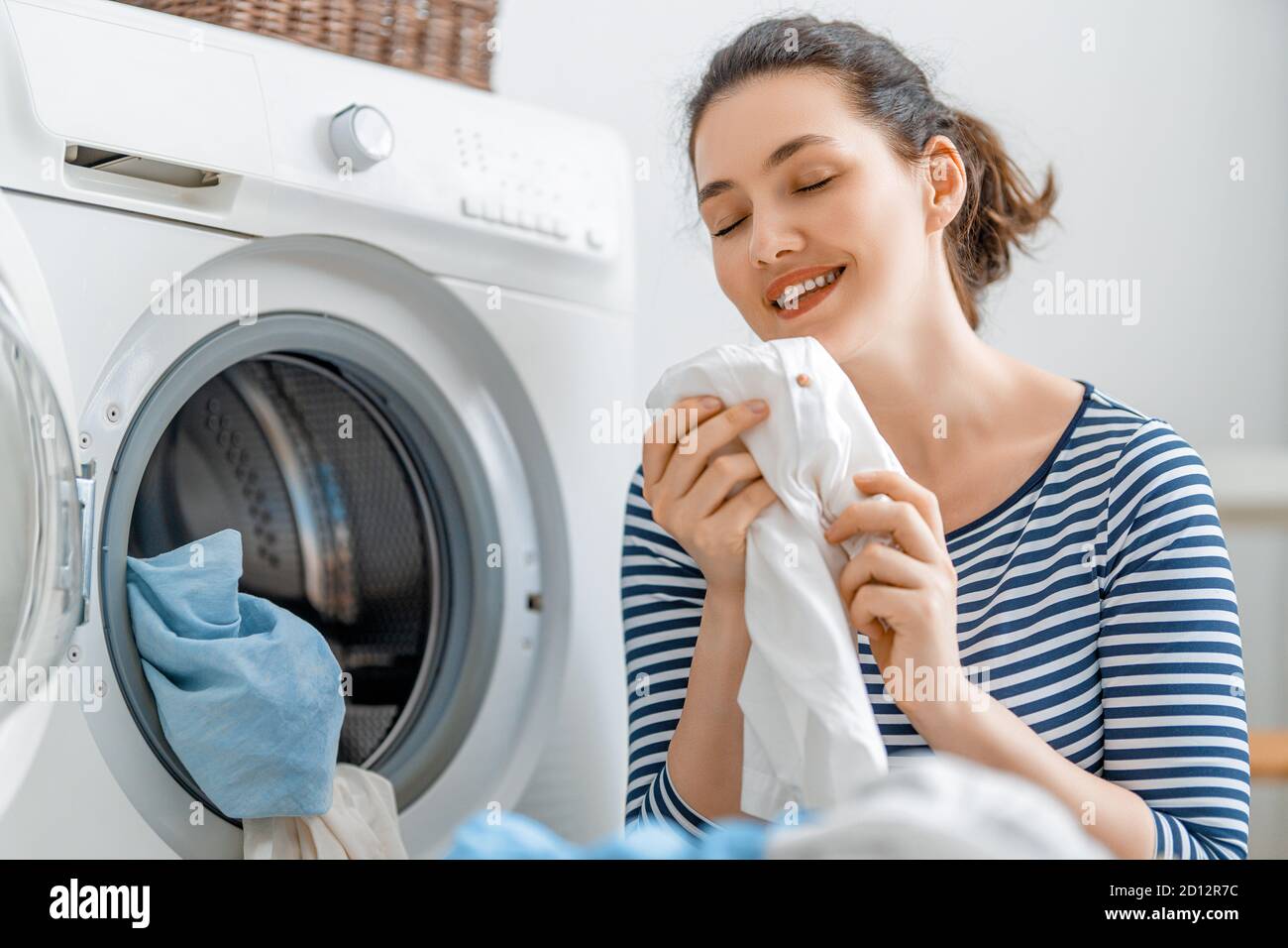 Beautiful young woman is smiling while doing laundry at home Stock Photo - Alamy