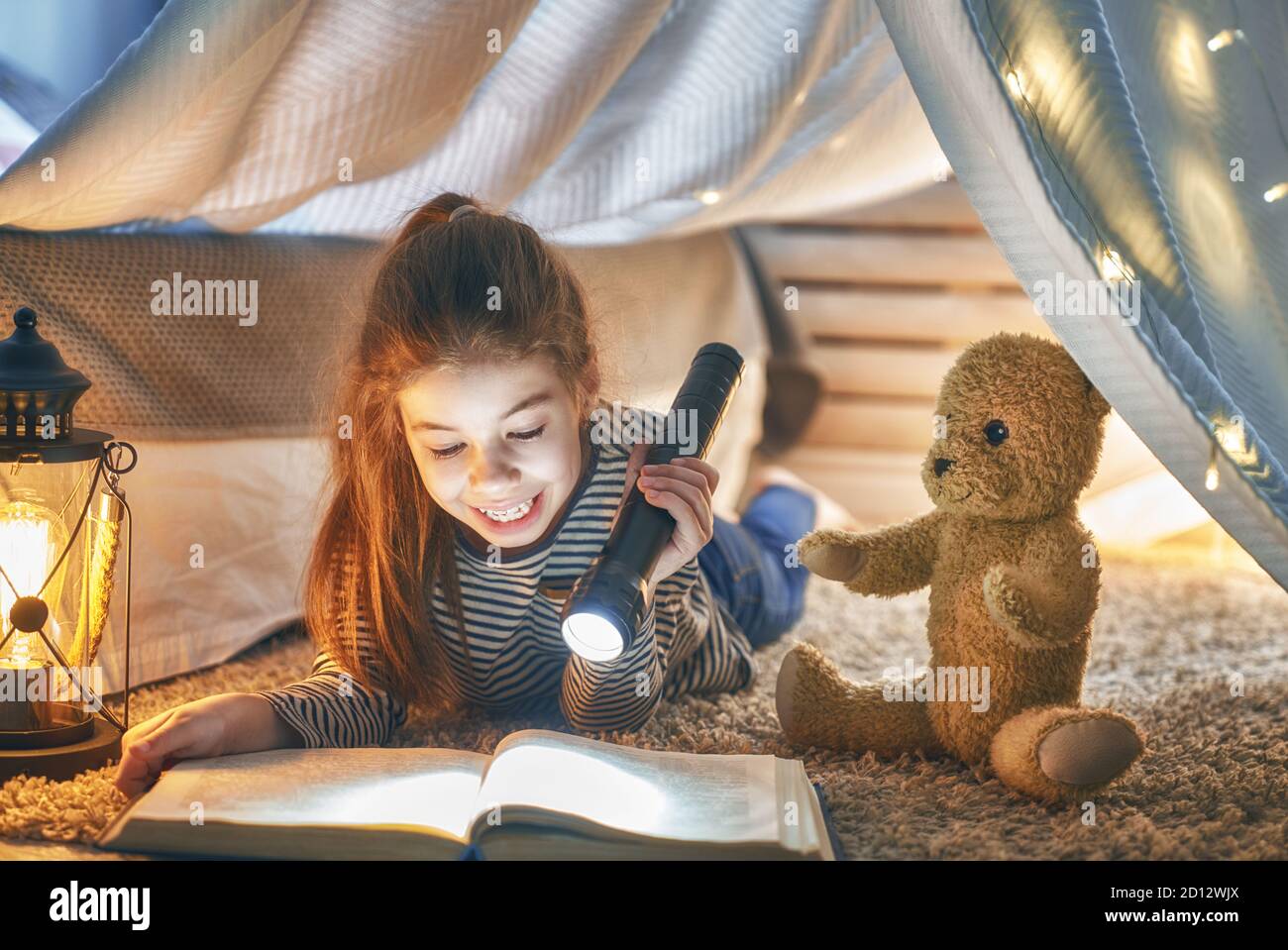 Cute little child is reading a book with flashlights in tent. Happy ...