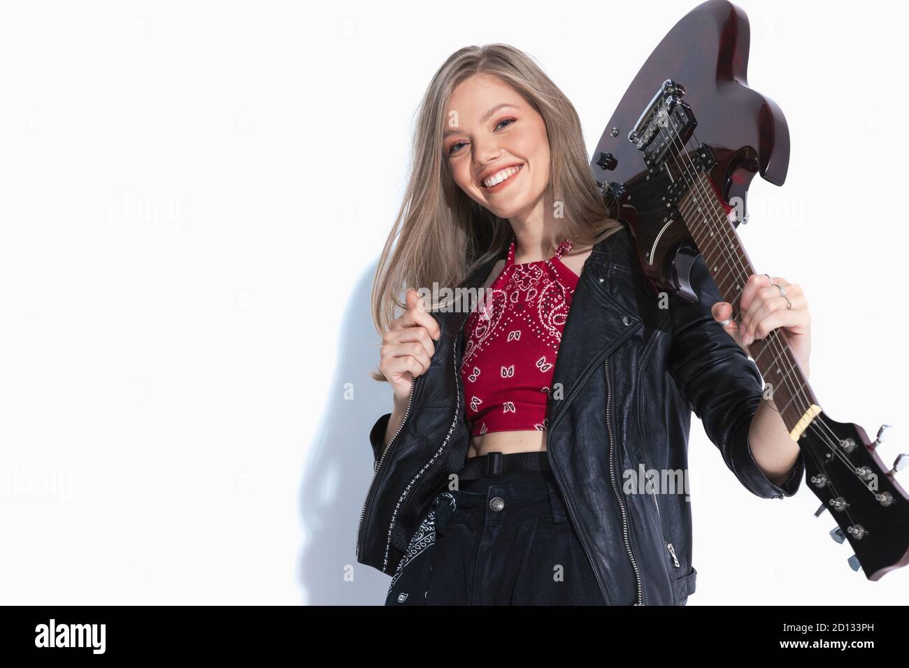 Cheerful musician holding guitar on shoulder and fixing jacket ...