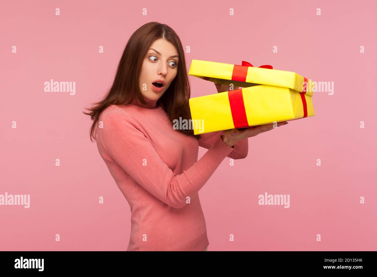 Amazed shocked brunette woman in pink sweater looking inside gift box ...