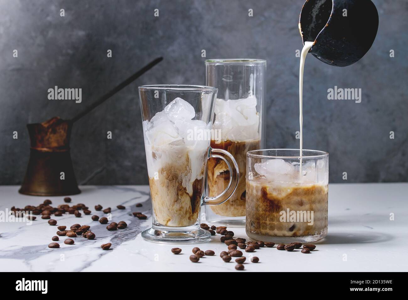 Iced coffee cocktail or frappe with ice cubes and pouring cream in ...