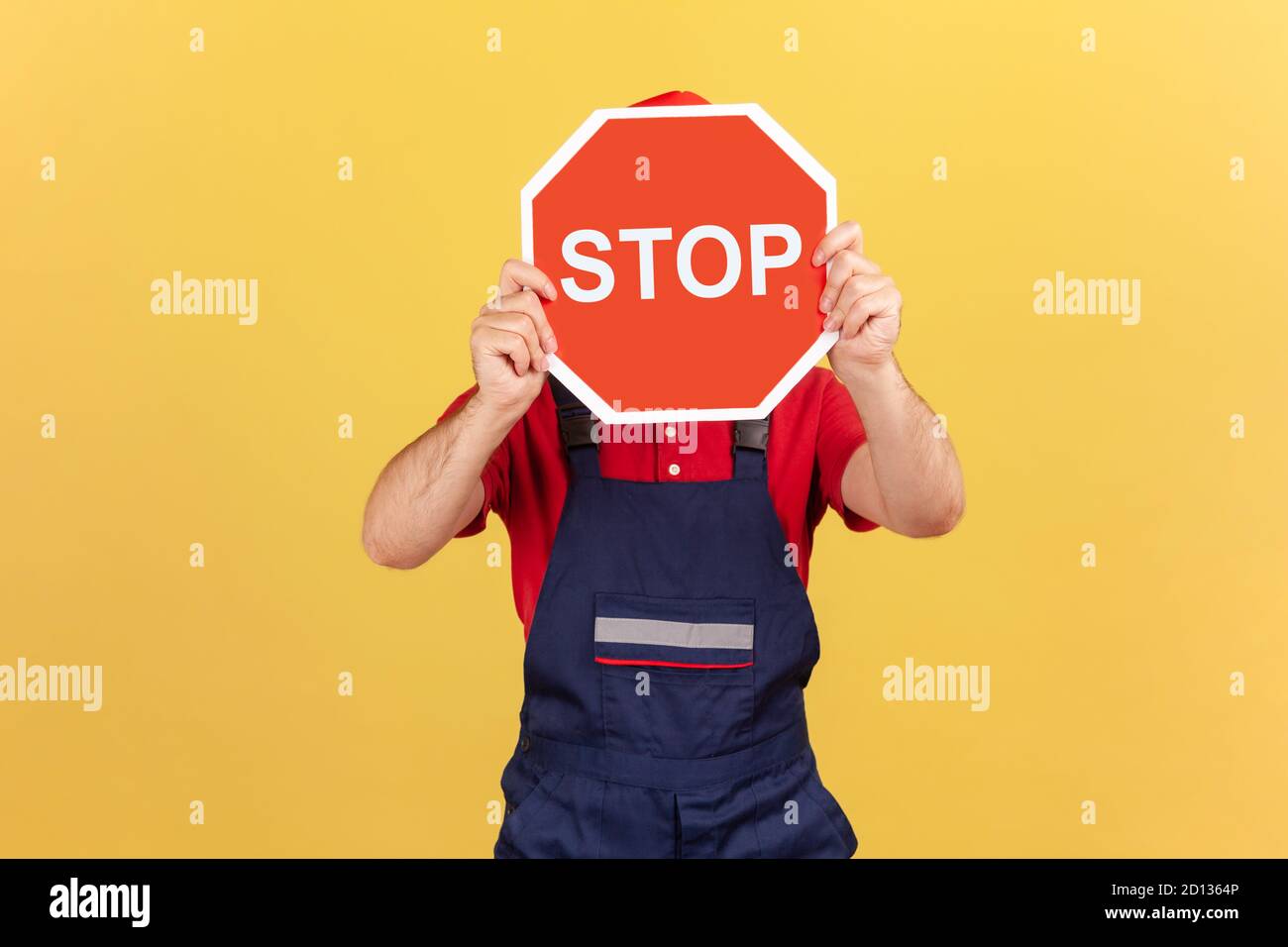 Man in blue overalls and red t-shirt covering face holding stop road ...