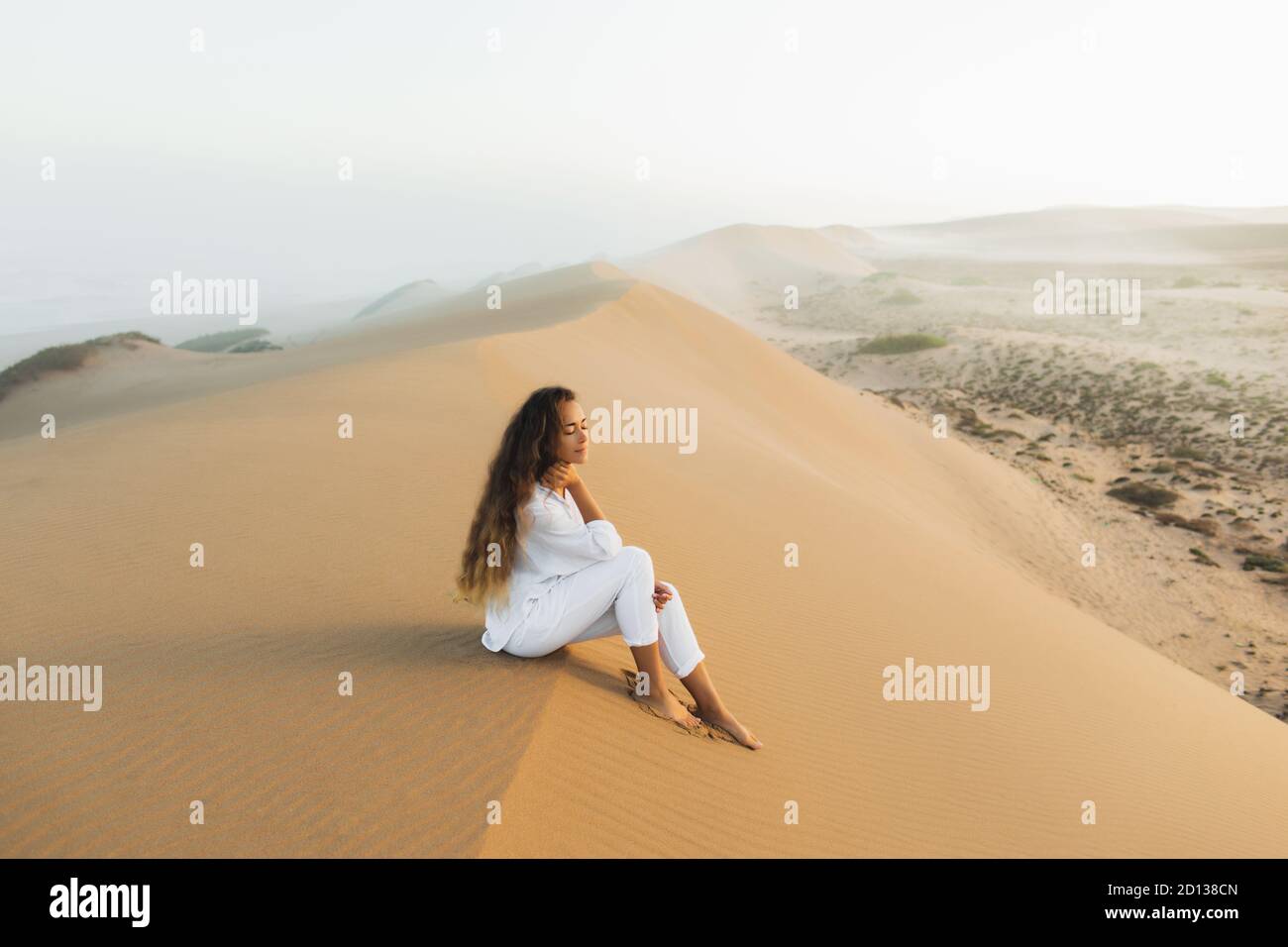 Beautiful brunette woman in white clothes relaxing on top of sand dune ...