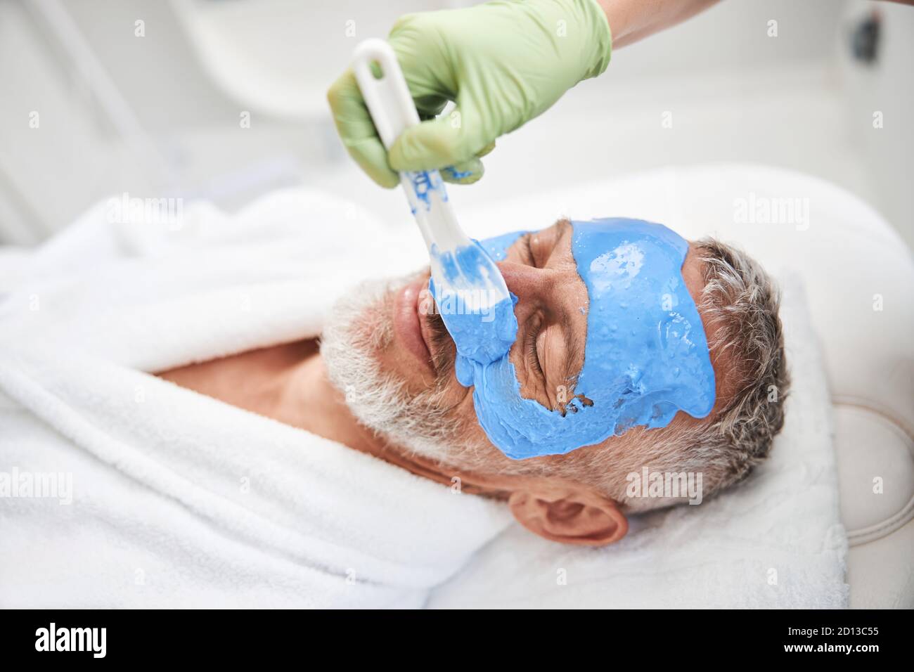 Spa worker putting blue cream on a person face Stock Photo - Alamy