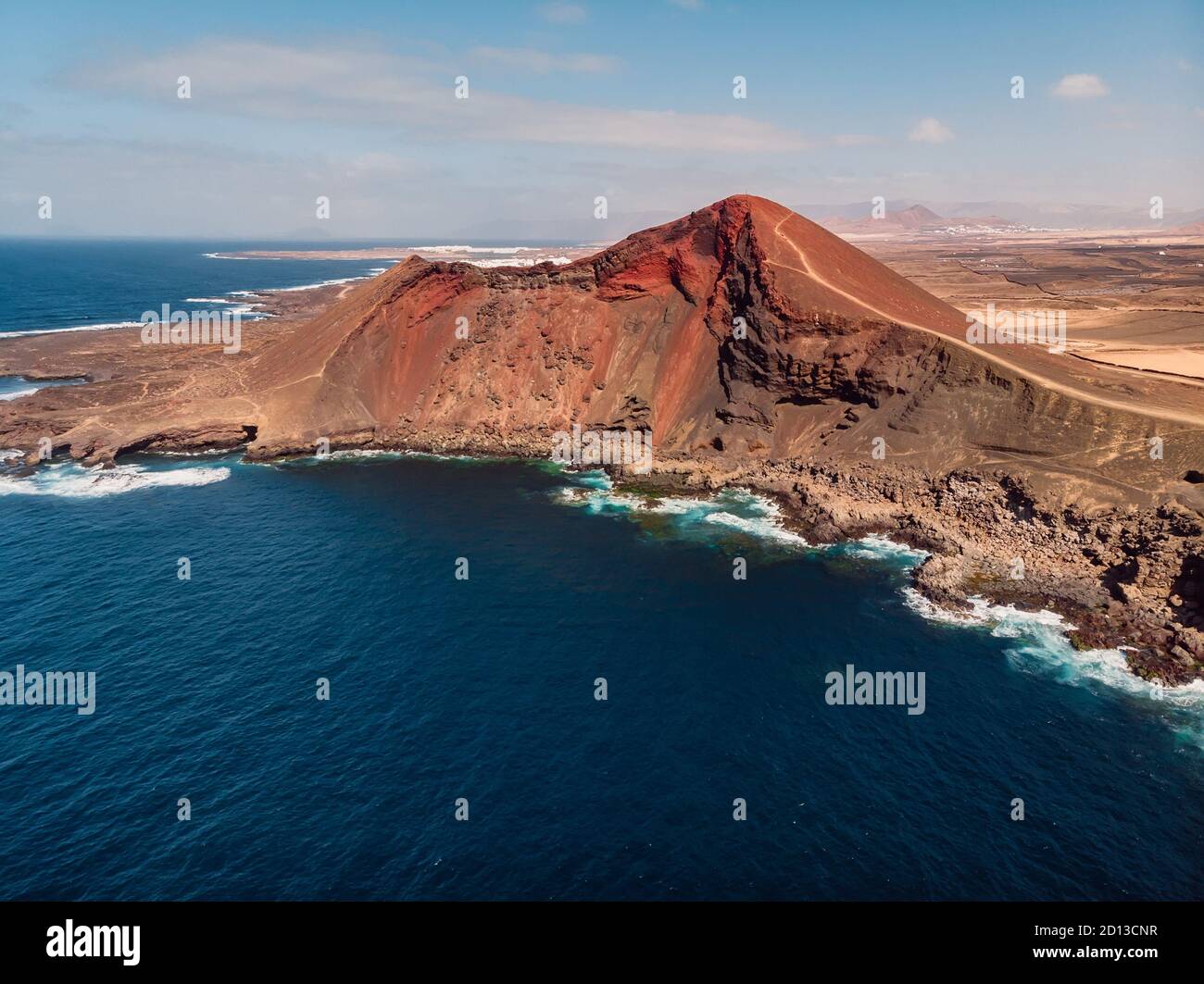 Old volcano with red rock and Atlantic ocean near La Santa, Lanzarote ...