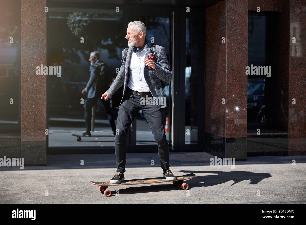 Grey-haired man riding a longboard in town Stock Photo - Alamy