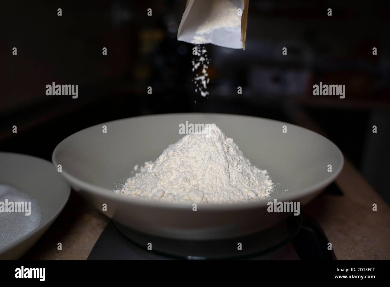 Pouring flour into a deep plate. Low light Stock Photo - Alamy