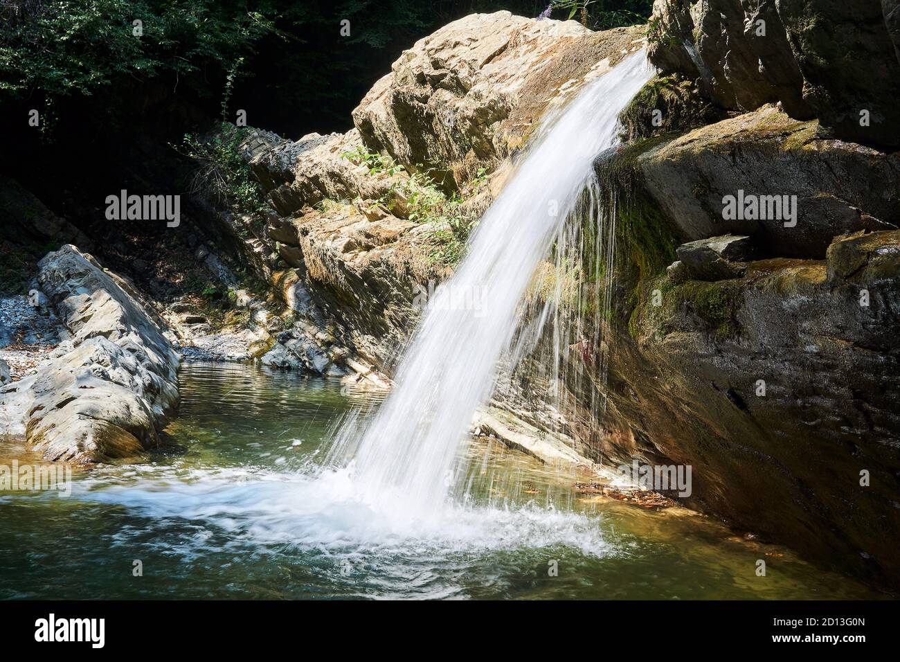 small clean waterfall falls from a rocky ledge in a wooded mountain ...
