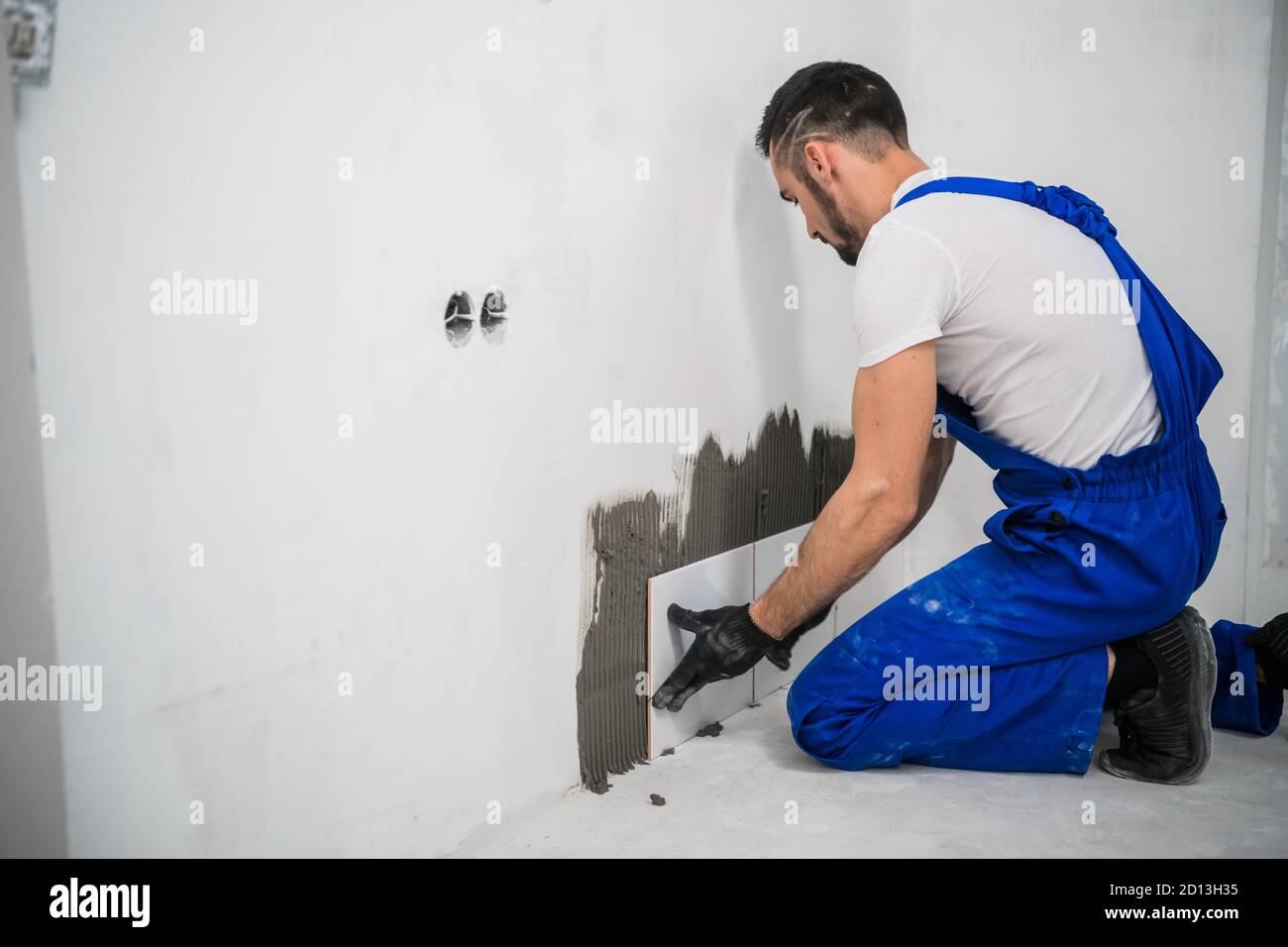 The general laborer attaches the tiles to the wall with cement. He is ...
