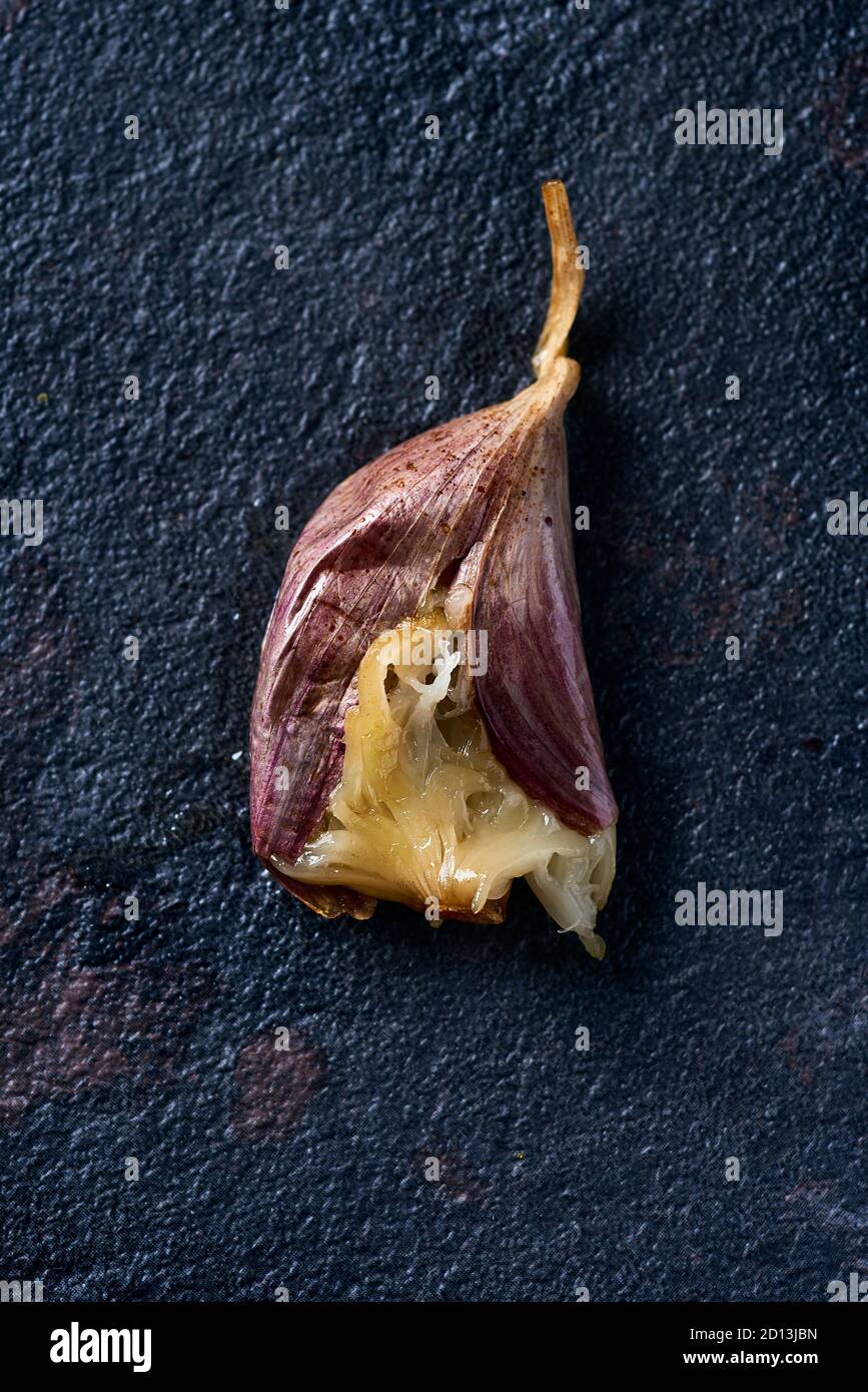 high angle view of an unpeeled roasted garlic clove on a black stone ...