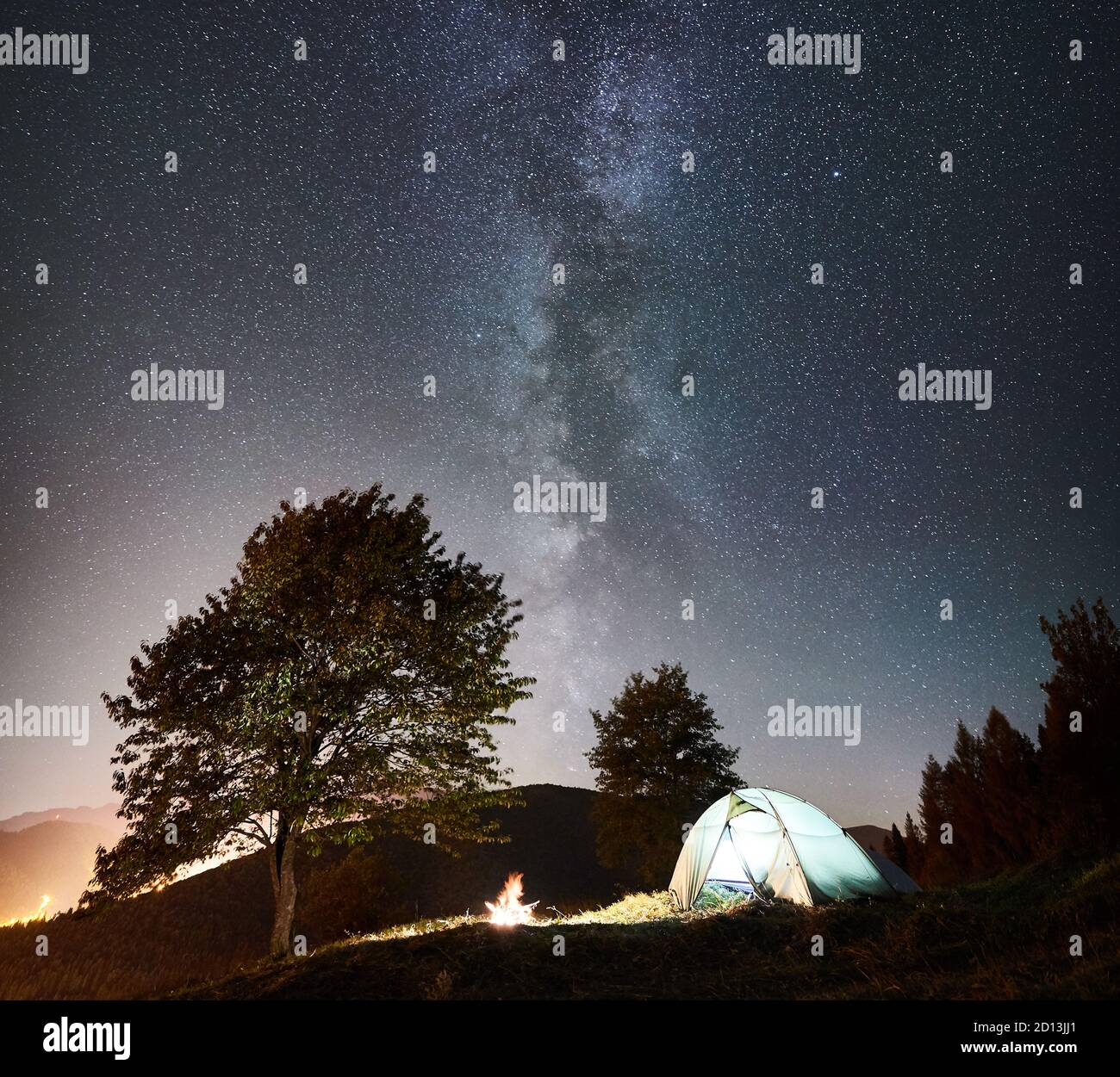 Tourist camping near forest at night. Illuminated tent and bonfire ...