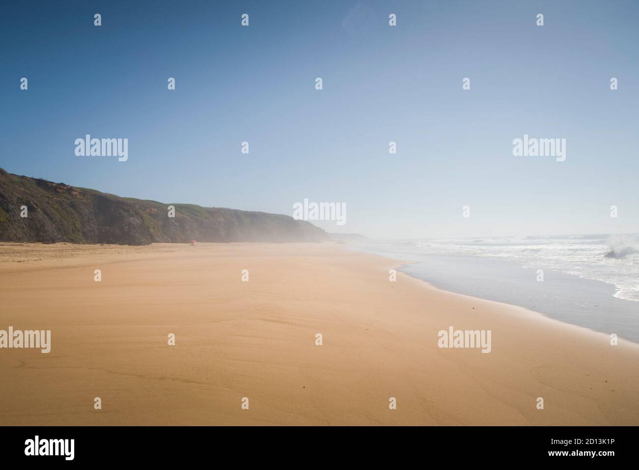 Empty vast beach with rock cliff entering the sand on the horizon and a ...