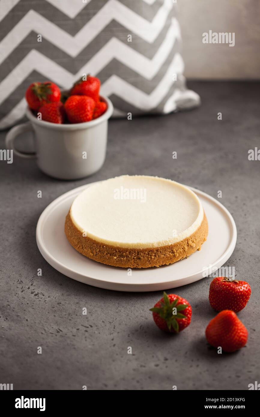Round cheesecake cake on a white plate with fresh red strawberries on a ...