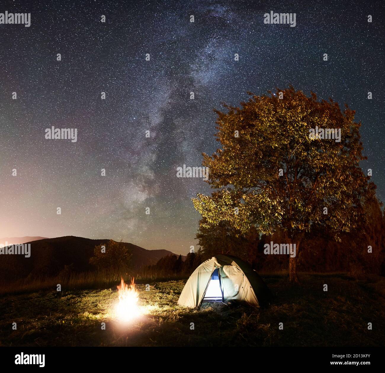 Tourist camping near forest at summer night. Glowing tent and bonfire ...