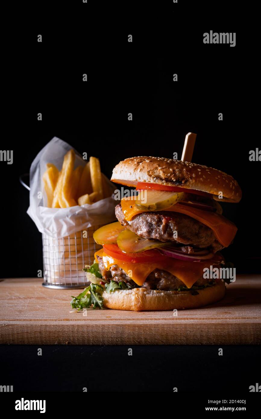 Closeup shot of a double beef burger and french fries on a wooden board ...