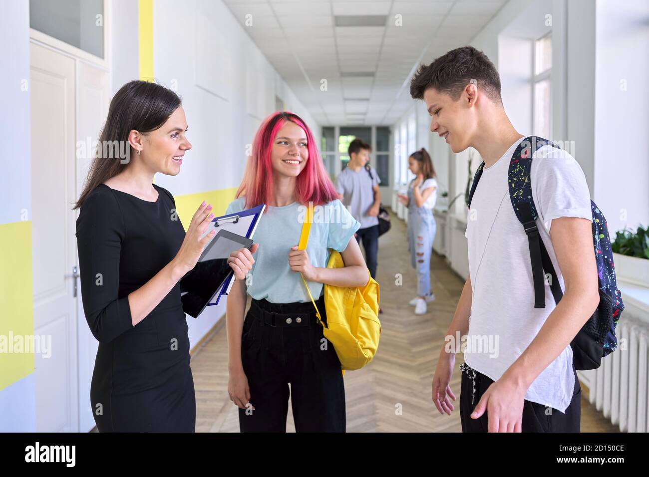 Group of teenage students talking to a female teacher in school ...