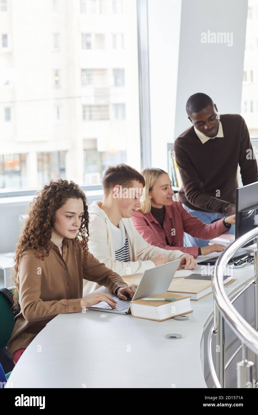 Vertical side view portrait of multi-ethnic group of students using ...
