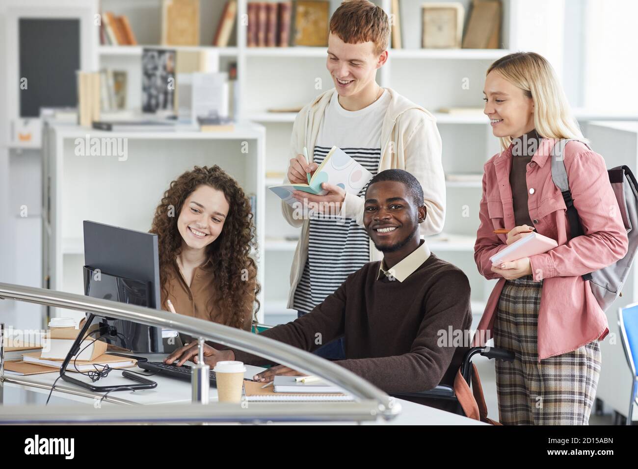Multi-ethnic group of students using telecommunication equipment while studying in college ...