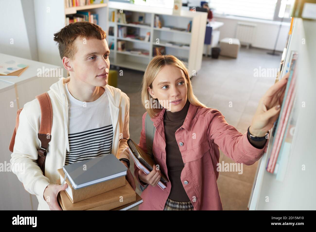 High angle portrait of two young people man and woman taking books off ...