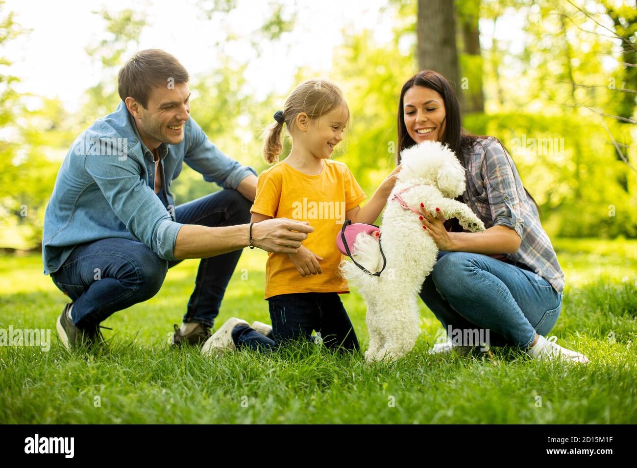 Beautiful happy family is having fun with bichon dog outdoors in the ...
