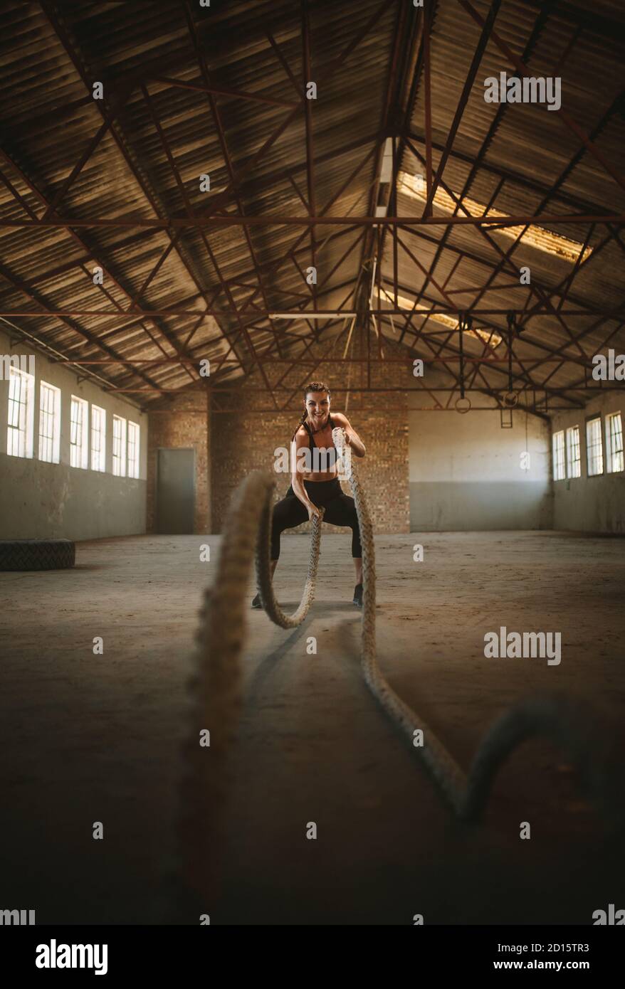 Tough woman using training ropes for exercise at gym inside old ...