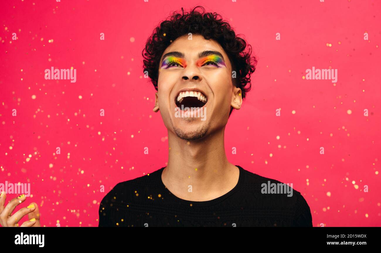 Cheerful gay man with glitters flying against red background. Excited ...