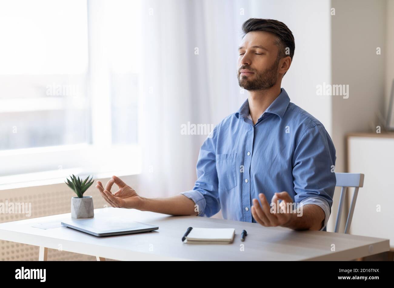Calm Millennial Businessman Meditating At Workplace, Practicing Yoga In ...