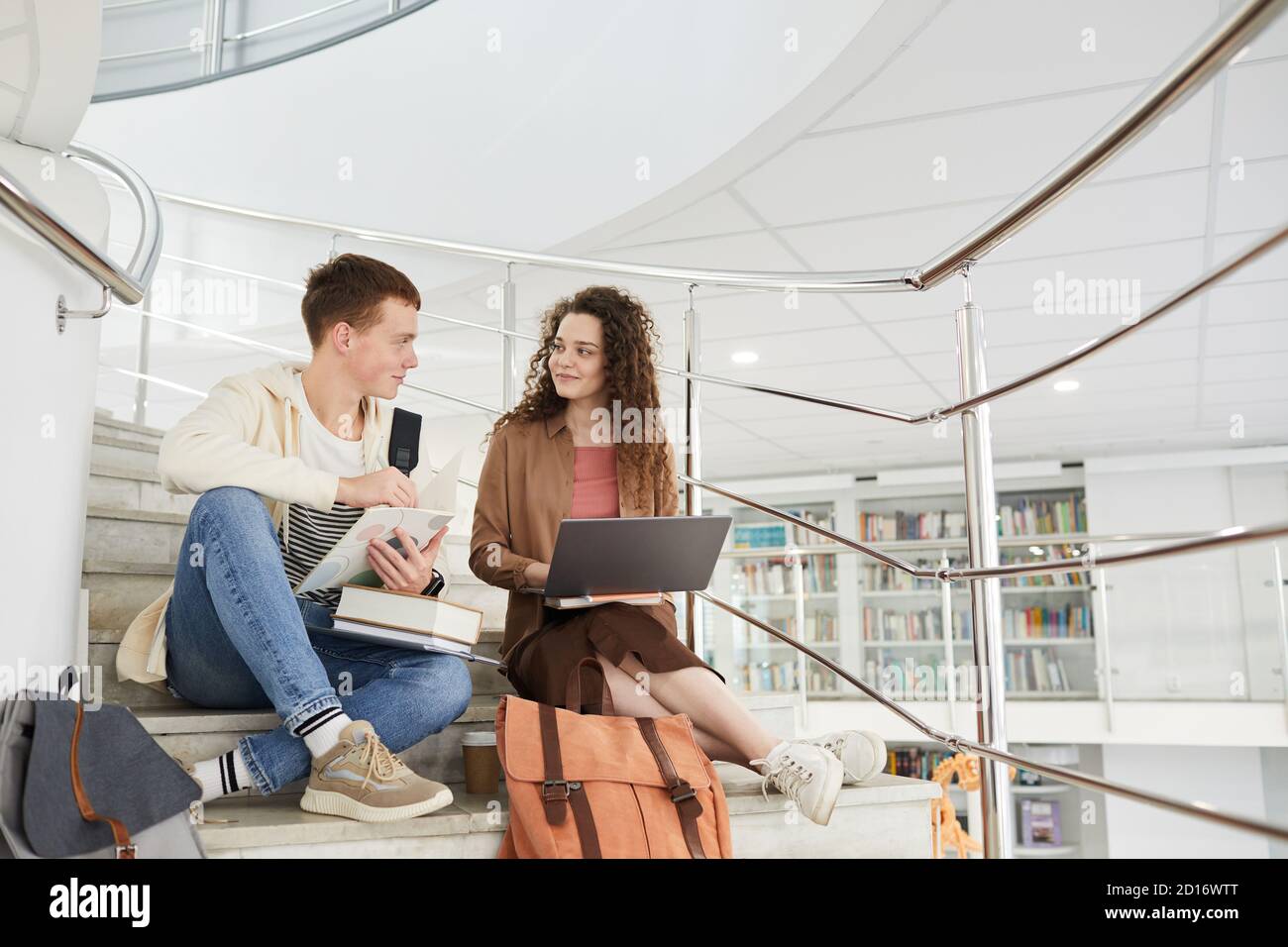 Wide angle view at two students sitting on stairs in college library ...