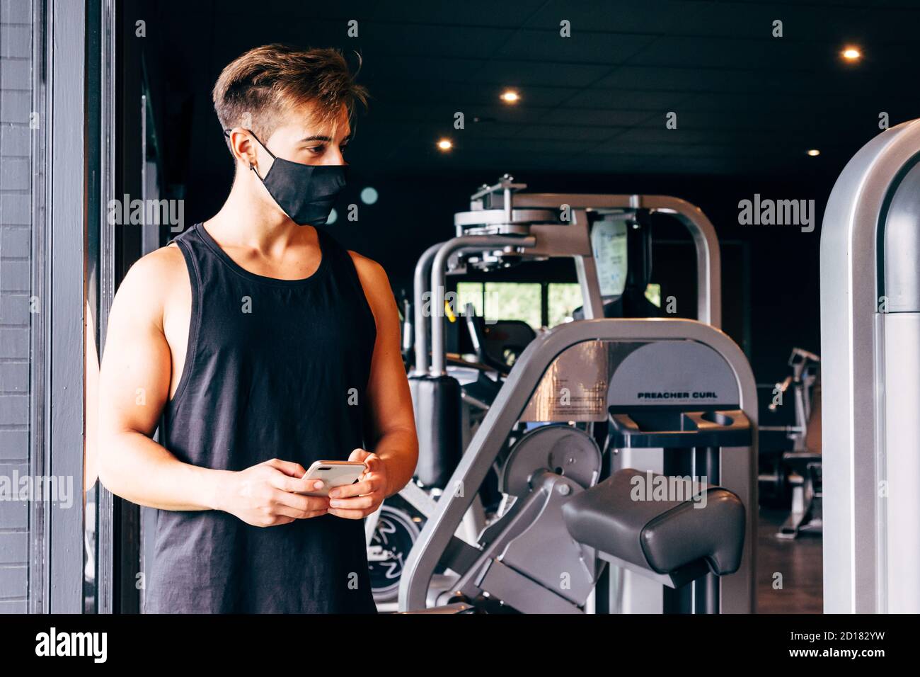 young man wearing face mask looks at his smartphone at the gym Stock ...
