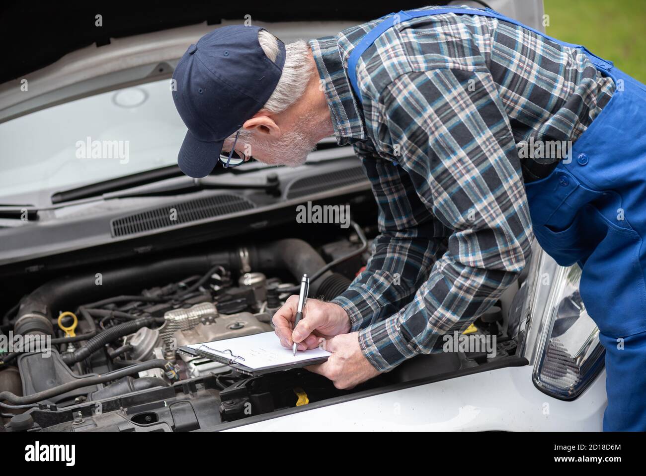 Car mechanic checking a car engine and writing on clipboard Stock Photo ...