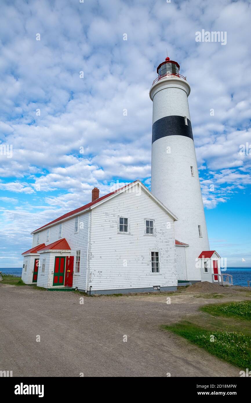 A tall circular red and white lighthouse with an attached light keeper ...