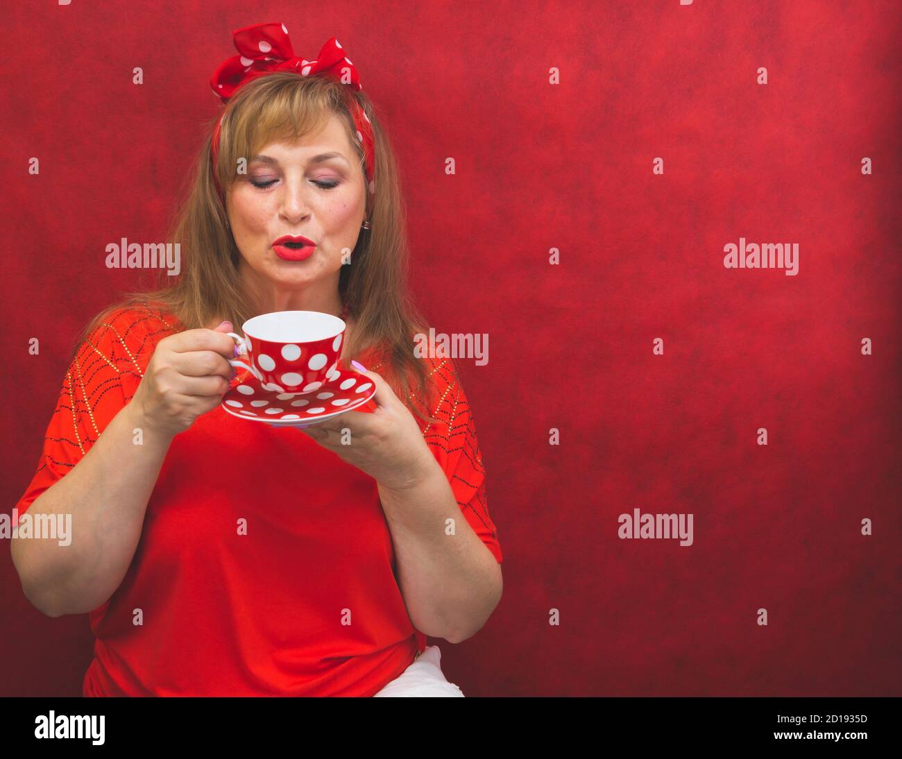 Woman in red posing on the red background. spotted cup with saucer in ...