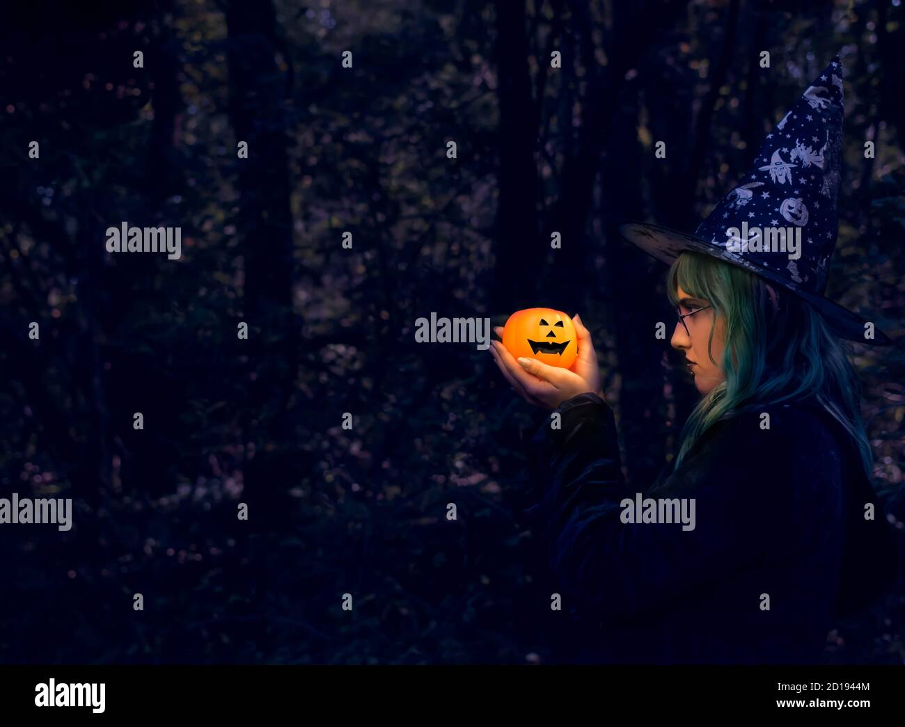Witch holding a magical pumpkin in woods. Girl in witch costume for ...