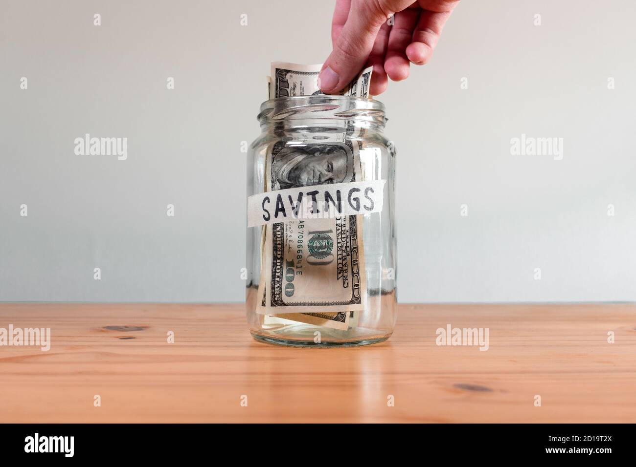 Hand of a person putting US Dollar bills in a glass jar labeled ...
