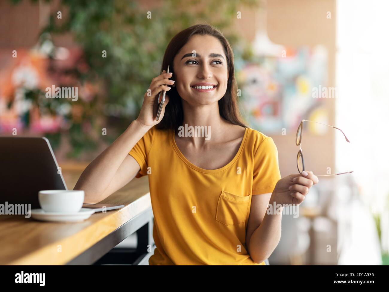Happy female student talking on phone while studying at cafe Stock ...