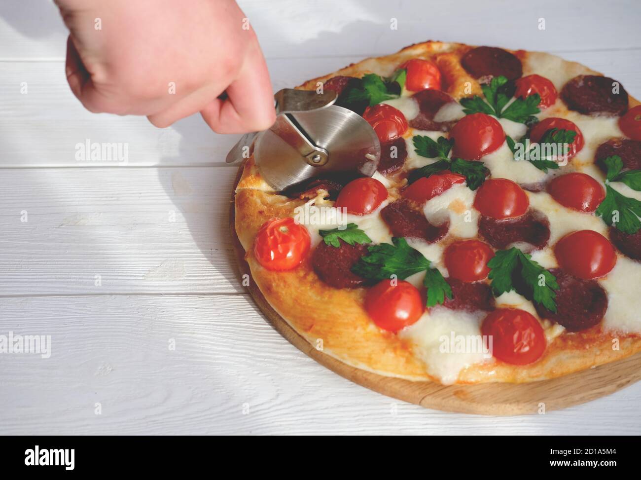 human hand with pizza cutter cut pizza in the kitchen. homemade italian ...