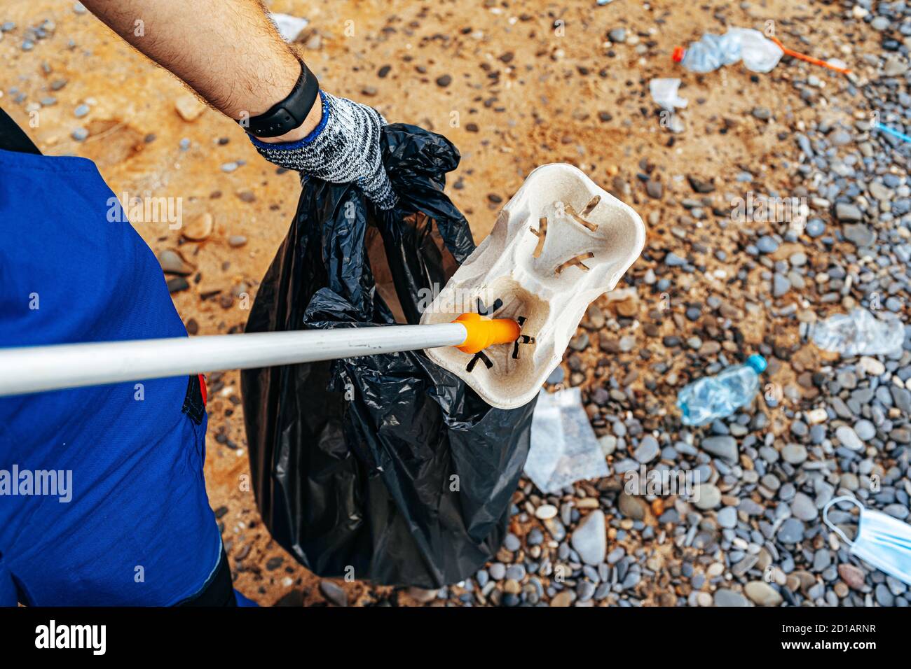 Close up photo of a man collecting garbage with a grabbing tool on the ...