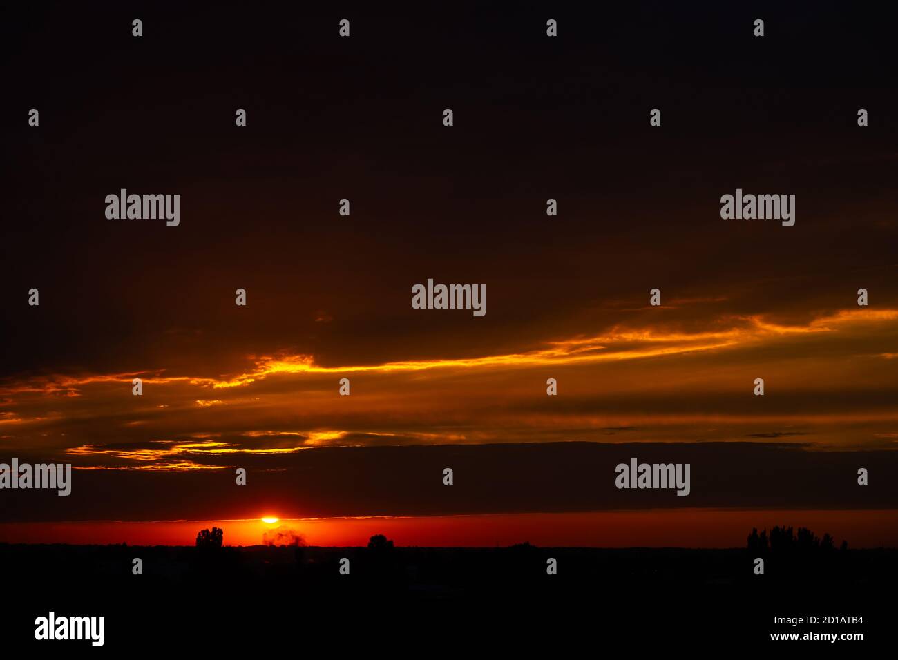 Heavy cloudy sky at sunset. Orange line of light between black clouds ...