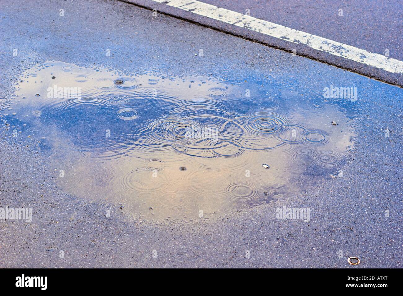 raindrops in a puddle on the asphalt with the reflection of clouds ...