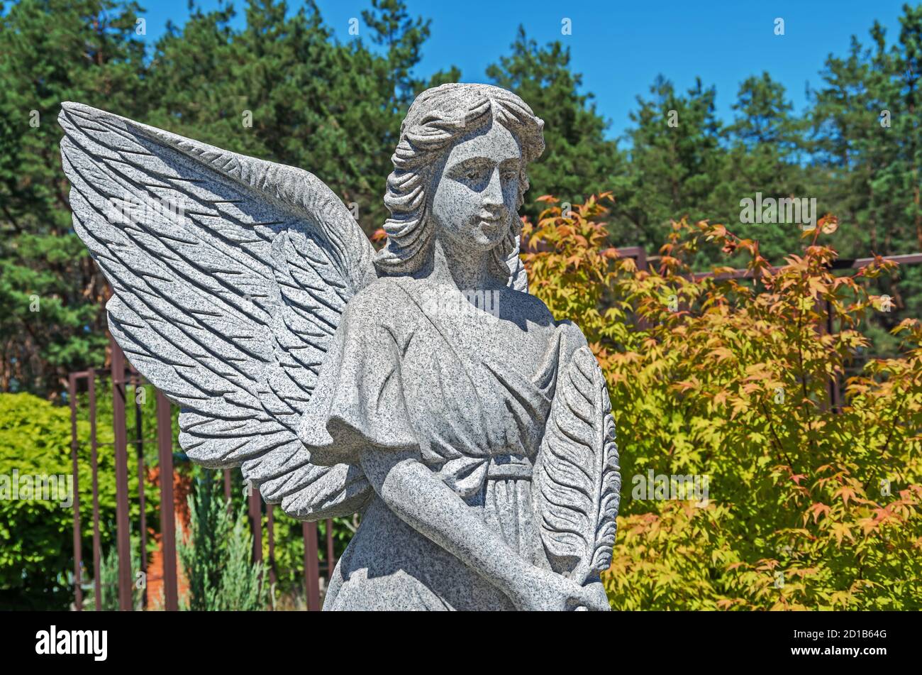 Statue grieving angel with wings against green trees and blue sky ...