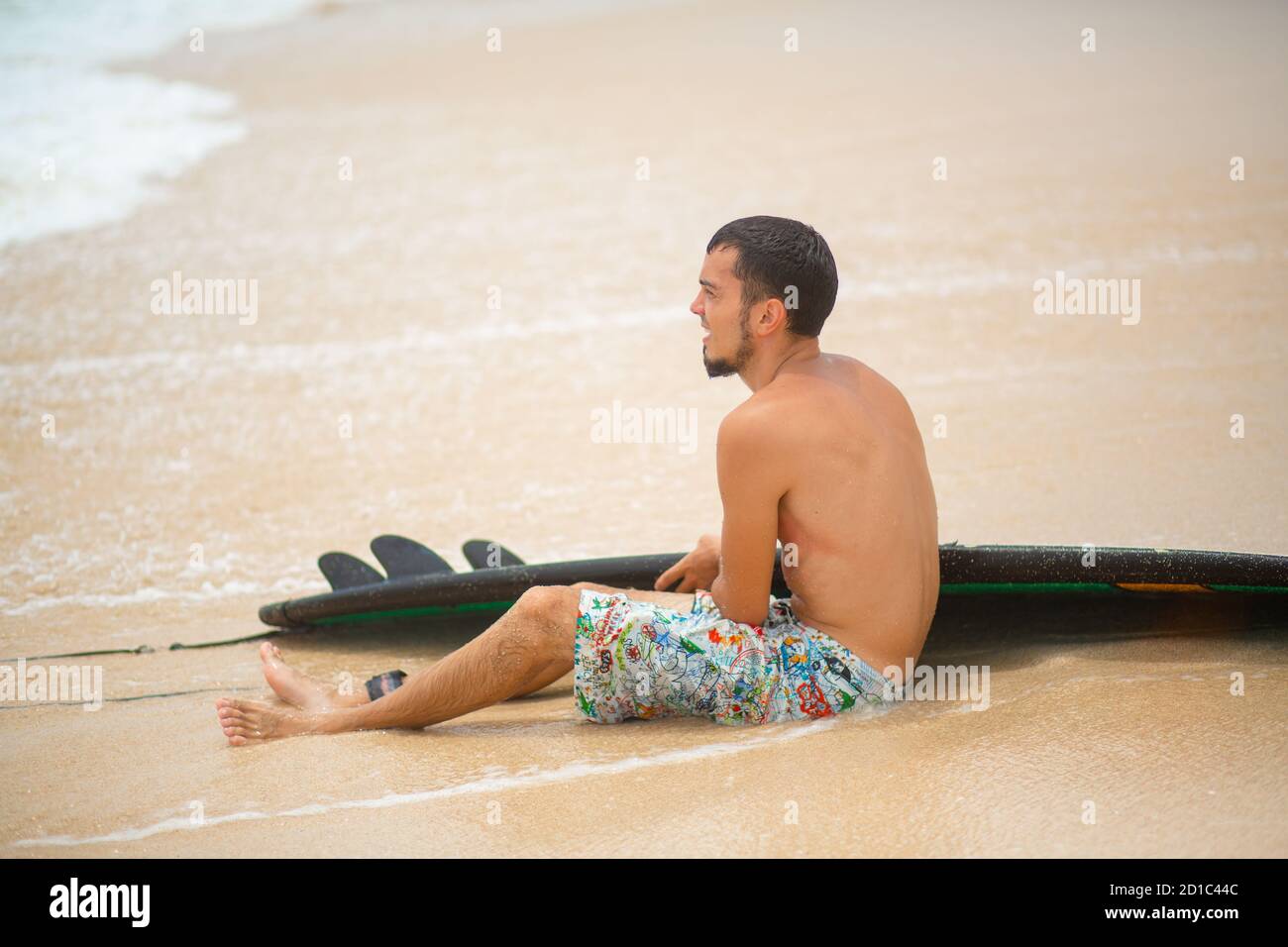 The guy is resting on a sandy tropical beach, after riding a surf ...