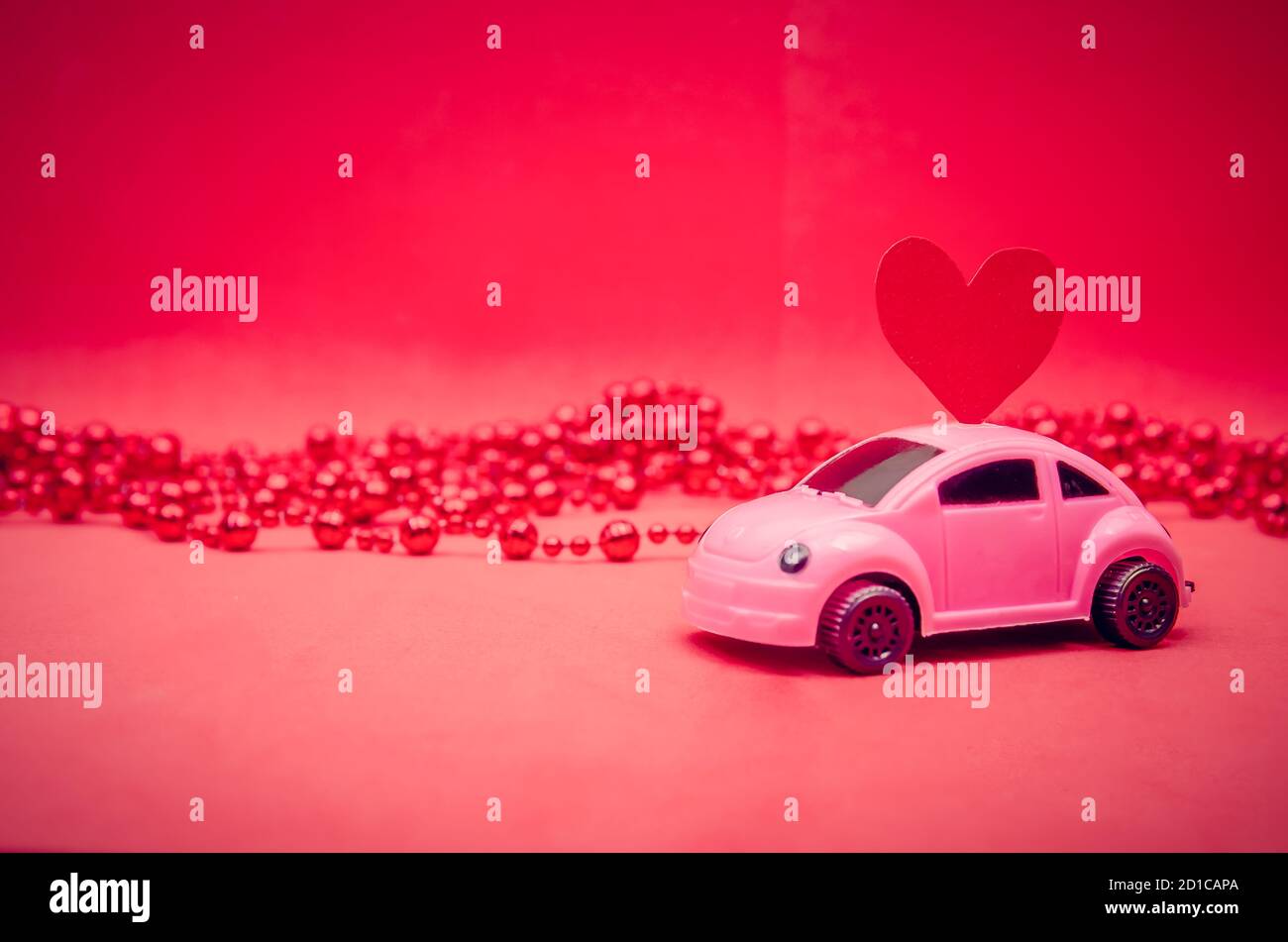 Small pink car with a red heart on the roof of the car on a red ...