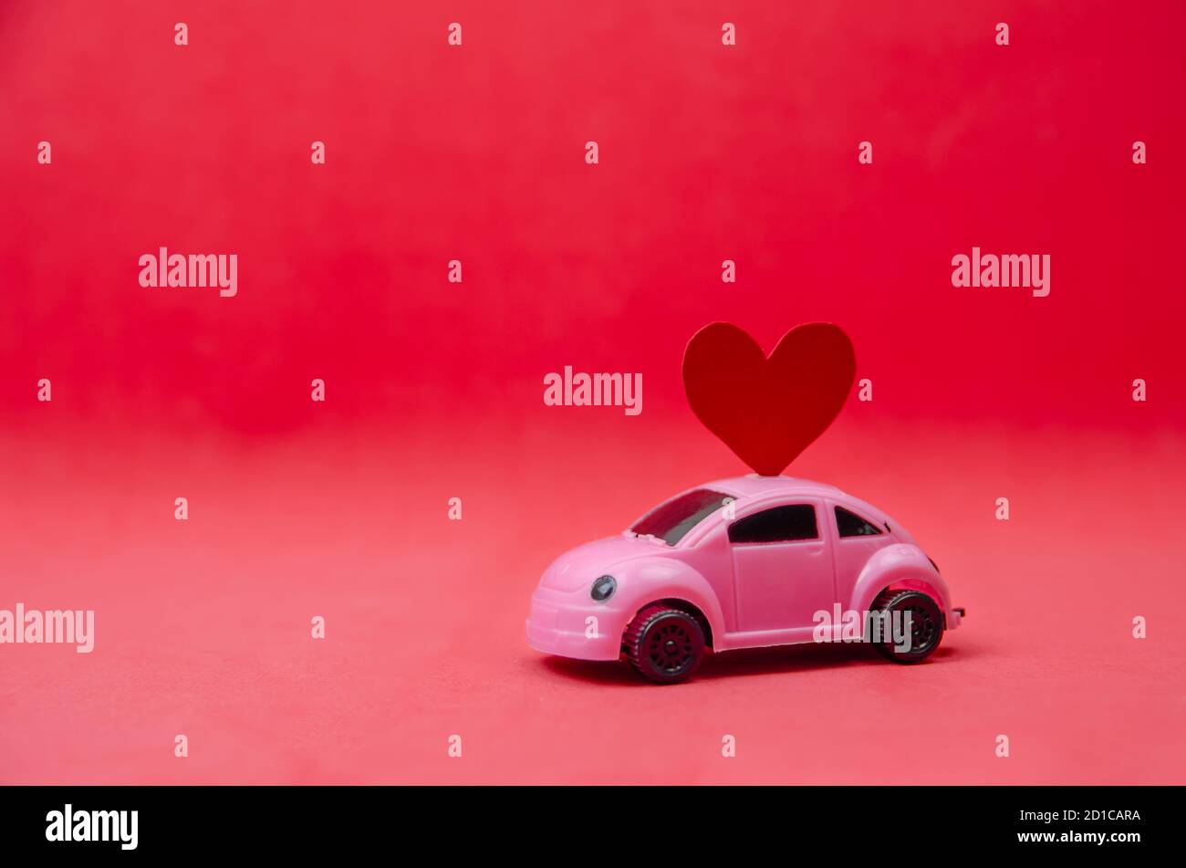 Small pink car with a red heart on the roof of the car with copy space ...