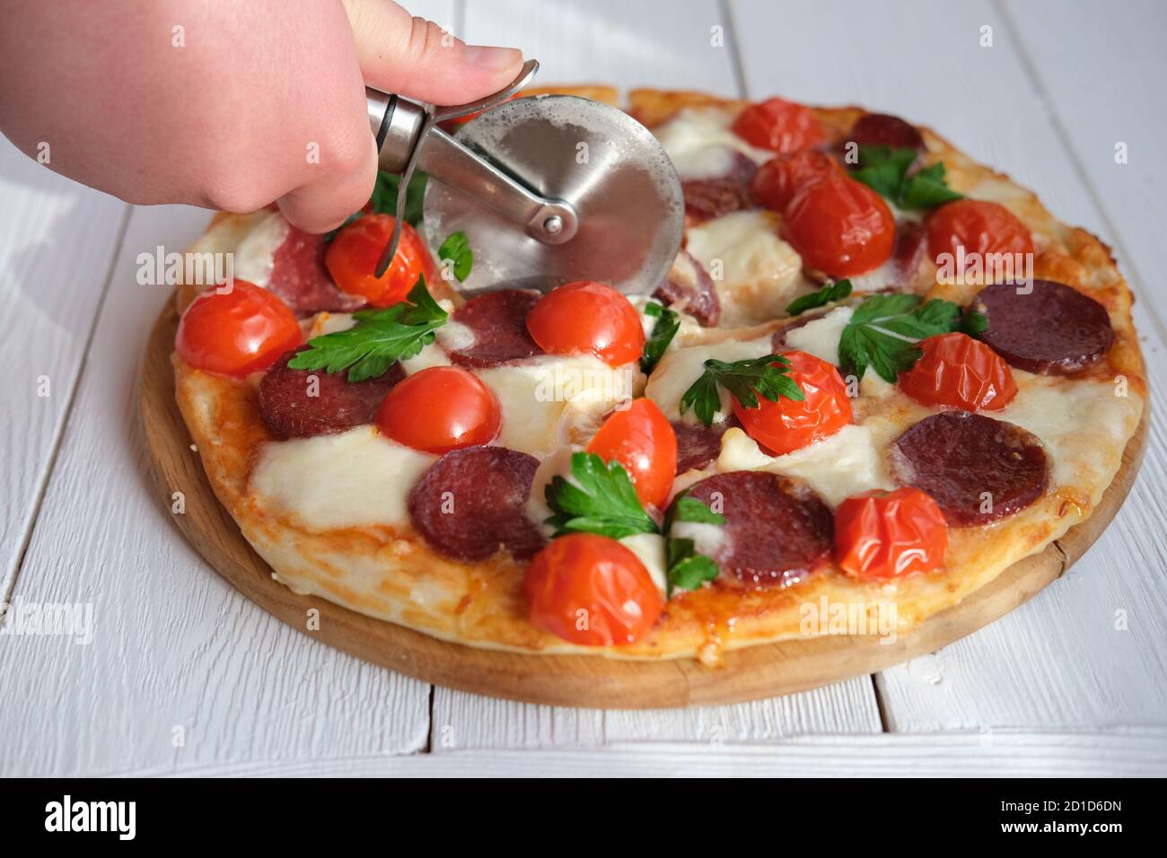 human hand with pizza cutter cut pizza in the kitchen. homemade italian ...