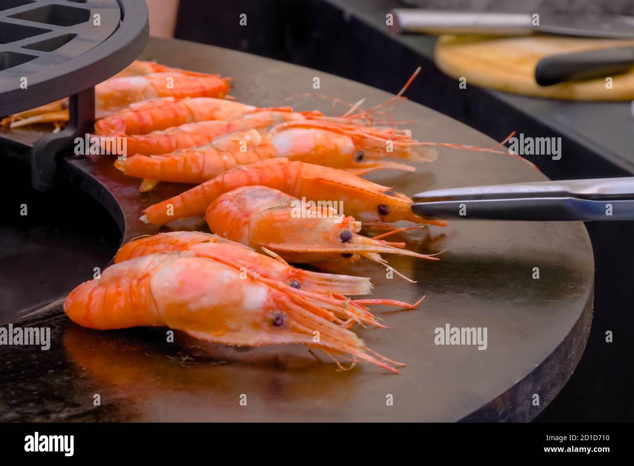 Chef grilling fresh red king prawns on round black brazier at summer ...