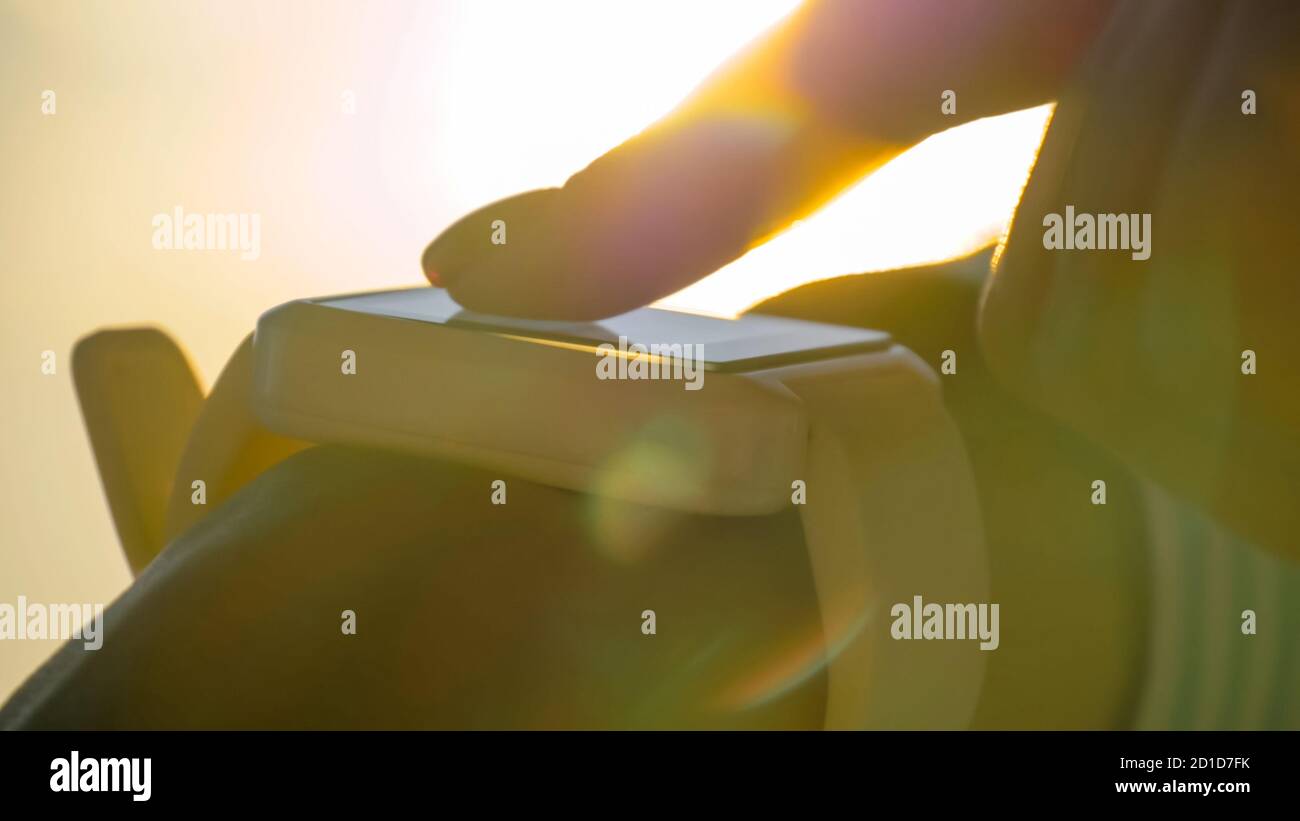Woman hand using wearable white smartwatch device against warm sunset ...